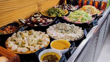 Buffet com diversos pratos, incluindo queijos, saladas e patês.
