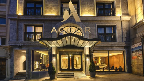 Entrada de hotel com logotipo destacado, área de acesso coberta e interior visível com assentos.