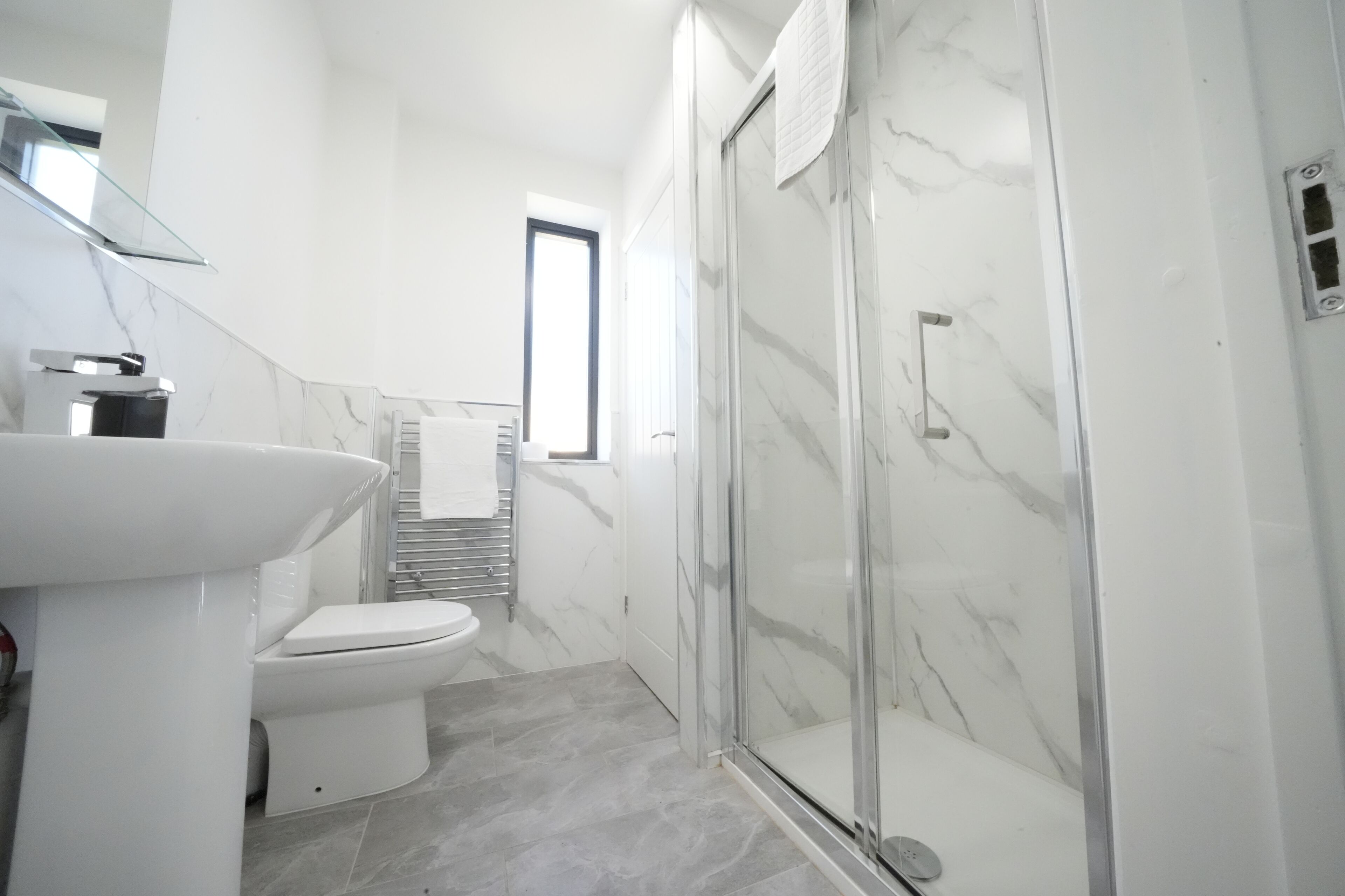 Casa de banho moderna com lavatório branco, sanita e cabine de duche com vidro.