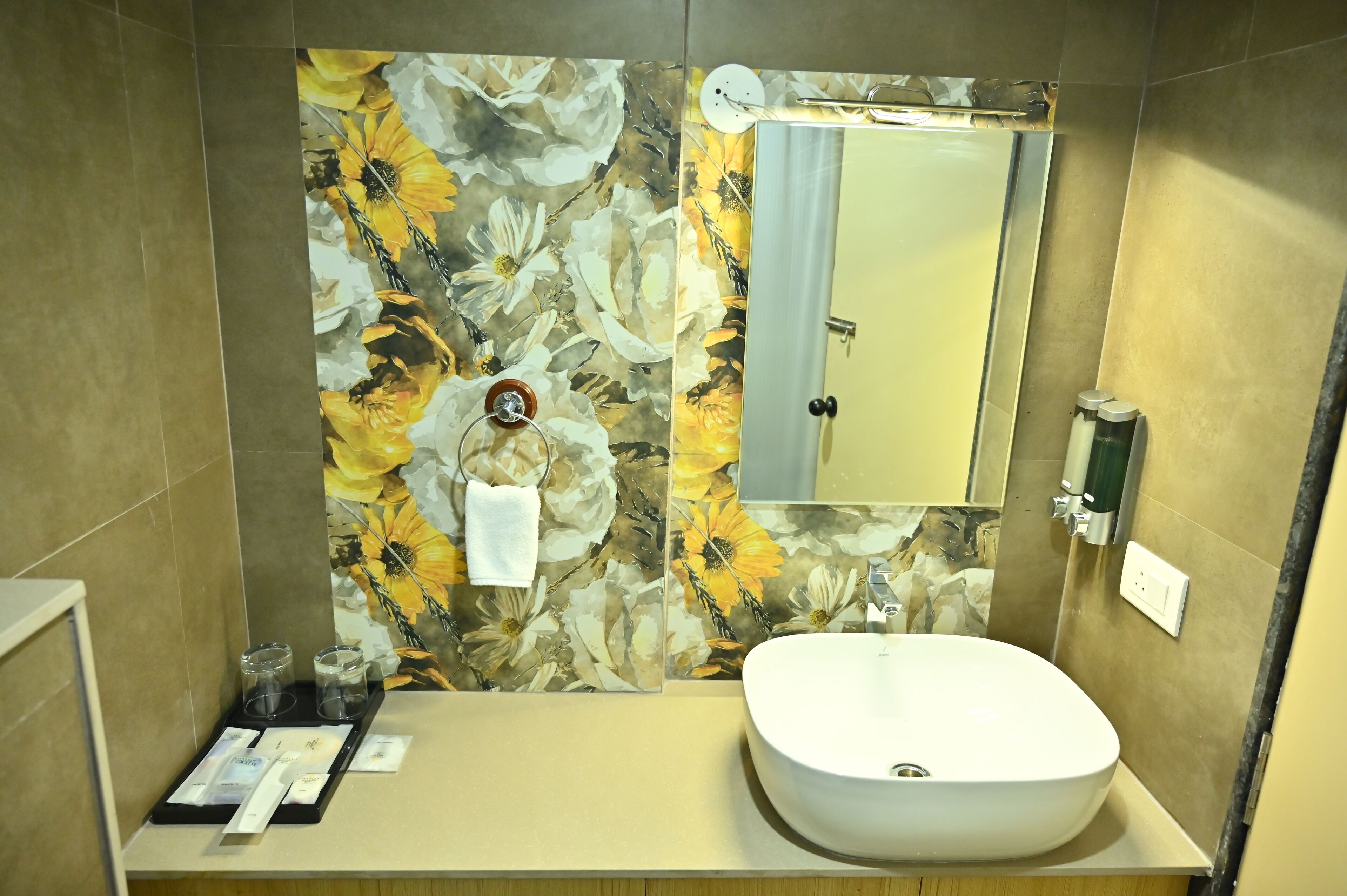 Casa de banho com papel de parede floral, pia, espelho e suporte para toalhas.