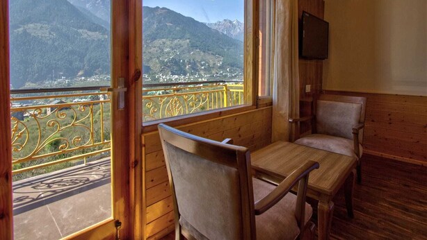 Varanda de madeira com mesa e cadeiras, com vista para uma paisagem montanhosa.