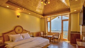 Quarto com painéis de madeira, uma cama grande, uma escrivaninha e uma cadeira. Há uma janela com vista para o exterior.