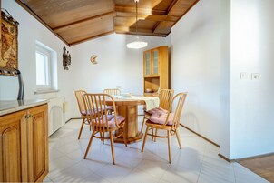 Uma área de refeições com mesa e cadeiras de madeira, um armário de madeira e um lustre.