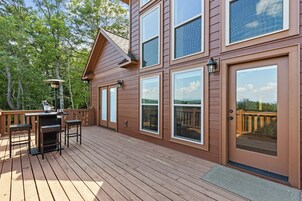 Um deck de madeira com mesa, cadeiras, janelas amplas e porta para o deck.