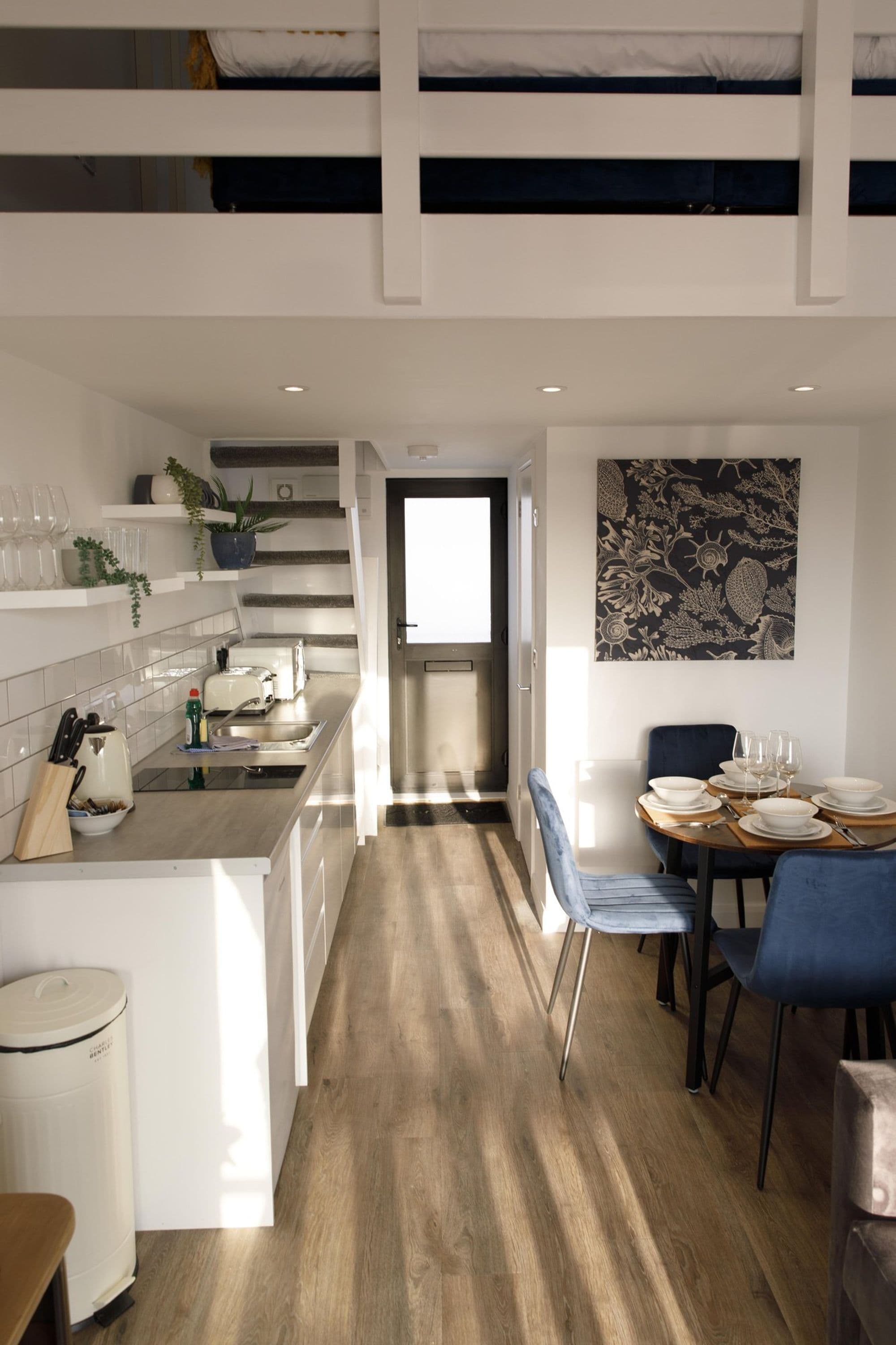 Uma cozinha moderna com uma ilha central, uma área de jantar com mesa e cadeiras, e uma escada que dá acesso a um andar superior.