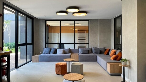 Uma sala de estar moderna com sofá seccional, mesinhas de madeira redondas e uma grande janela que proporciona iluminação natural.
