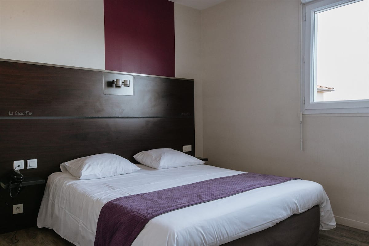 Quarto com cama, mesa de cabeceira, parede de destaque vermelha e janela.