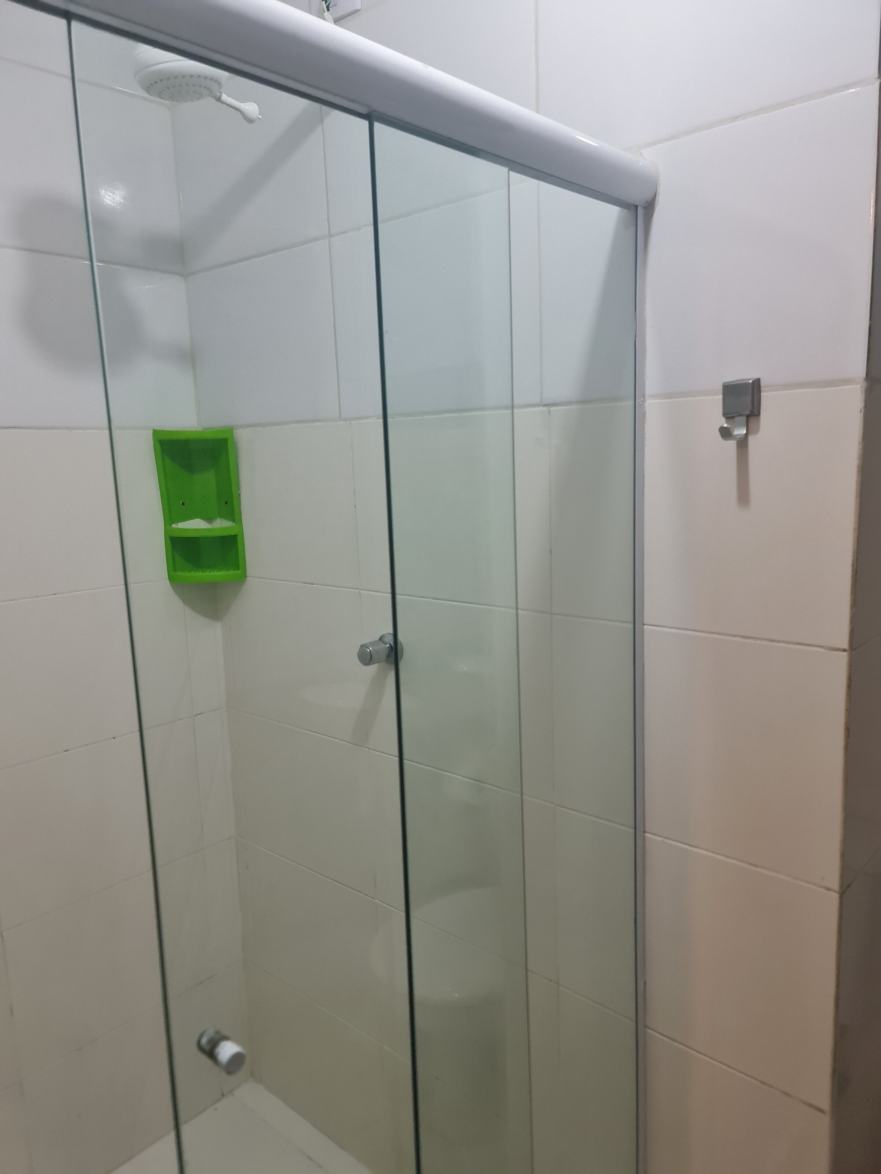 Box de chuveiro com paredes revestidas de azulejos brancos, um saboneteira verde e uma maçaneta de metal.