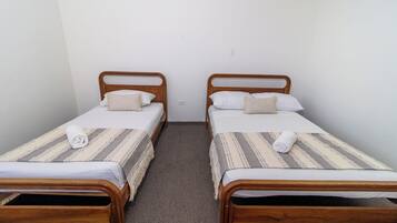 Duas camas de solteiro com estrutura de madeira e roupa de cama listrada, um piso coberto por carpete e uma parede branca sem adornos.