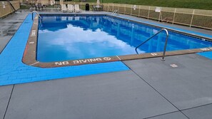 Uma piscina com borda azul, um aviso de proibição de mergulhos e cadeiras de espreguiçadeira ao redor.