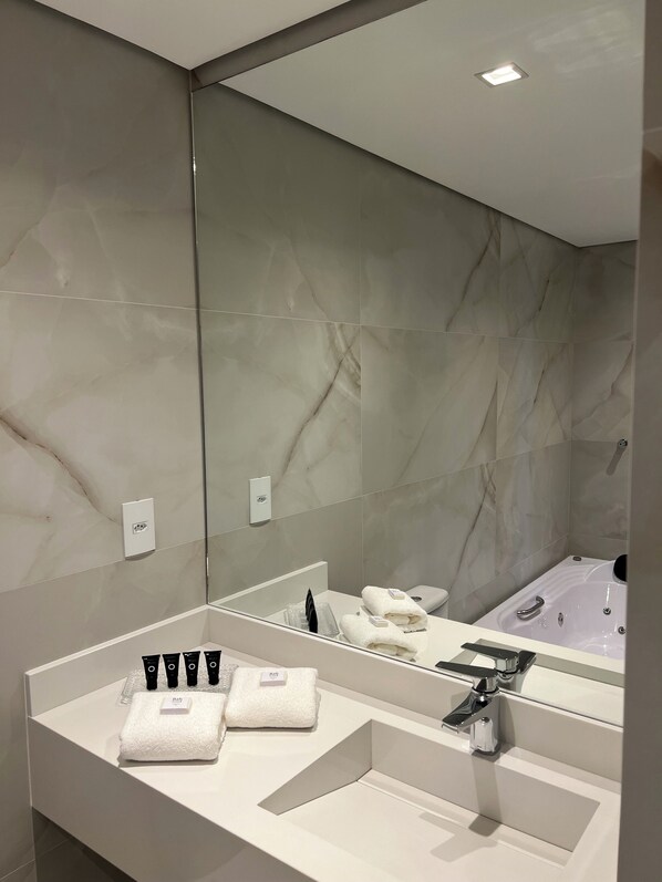 Uma casa de banho moderna com um espelho grande, uma banheira e uma cómoda com artigos de higiene pessoal.