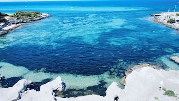Paisagem costeira com águas azul-claras, formações rochosas e uma linha de costa distante.