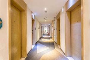 Corredor de hotel com portas de madeira, piso carpetado e iluminação embutida.