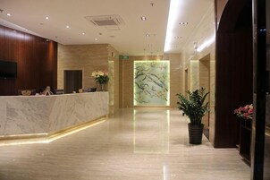 Um saguão de hotel com balcão de recepção, uma grande obra de arte abstrata na parede e plantas em vasos.