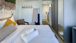 Quarto de hotel com cama, uma cadeira, um cabideiro e um guarda-roupa.