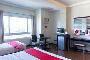 Quarto de hotel com duas camas, uma escrivaninha, televisão e janela com cortinas.