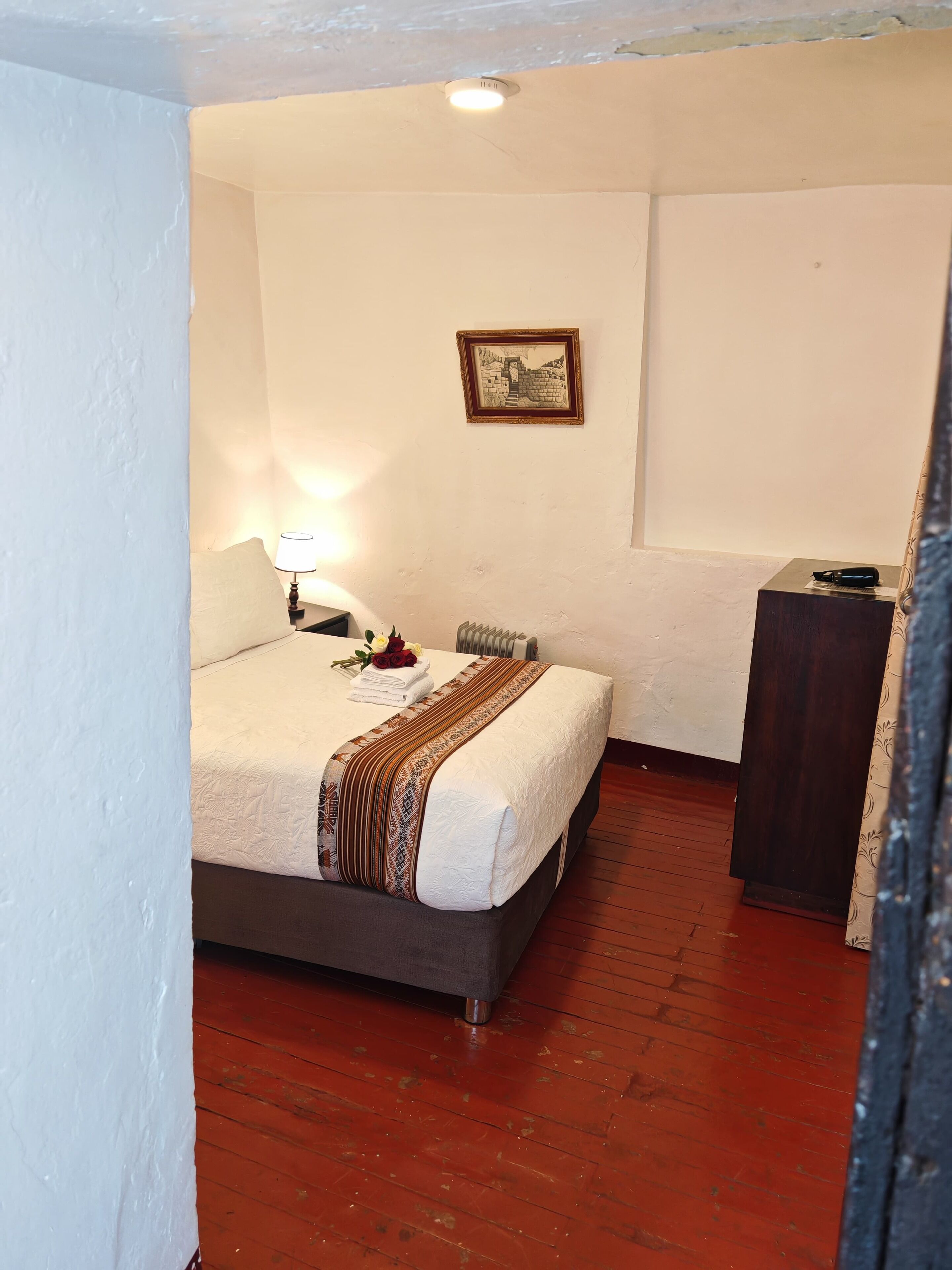 Cama bem arrumada com manta estampada, luminária de cabeceira e quadro na parede.