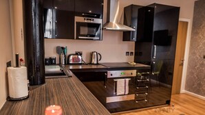 Cozinha moderna com armários pretos, eletrodomésticos de aço inoxidável e bancada de madeira.