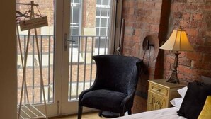 Quarto de hotel com cama, uma cadeira, abajur e vista para o exterior.