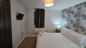 Quarto de hotel com uma cama grande, televisão de tela plana na parede, janela com cortinas, mesa de cabeceira com abajur e parede com textura.