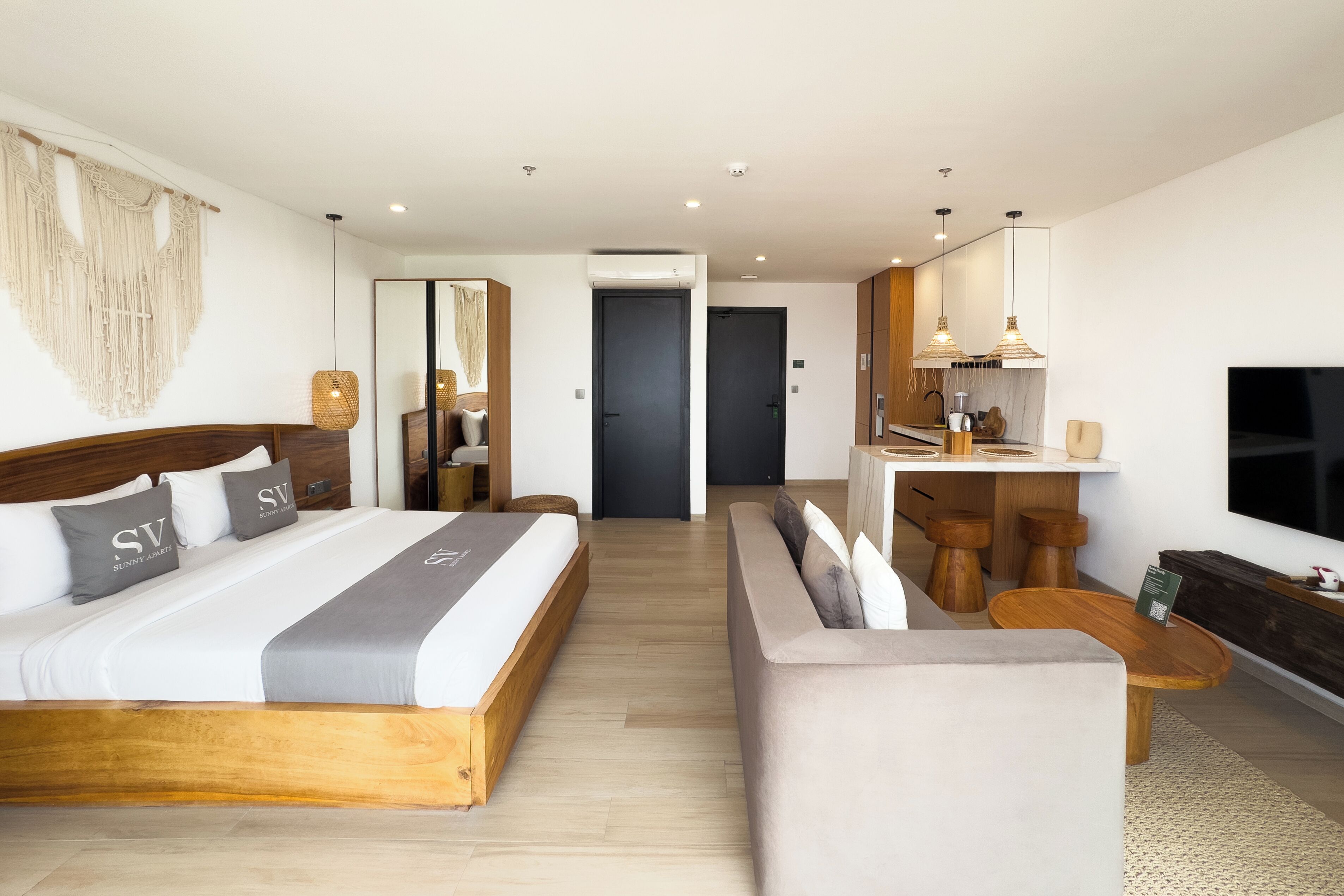Quarto de hotel moderno com uma cama grande, um sofá, uma televisão, uma escrivaninha e um espelho.