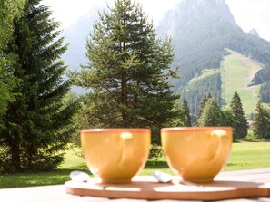 Duas chávenas amarelas sobre um tabuleiro de madeira, com uma paisagem de montanhas ao fundo.