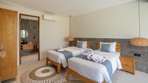 Quarto moderno com duas camas, um guarda-roupa de madeira, banheiro com espelho e uma parede com detalhes em pedra.