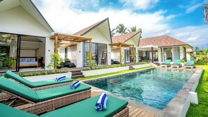Uma casa moderna com piscina, espreguiçadeiras verdes e um jardim bem cuidado.