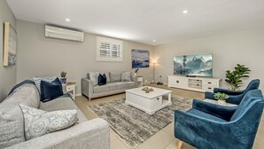 Uma sala de estar moderna com um sofá cinzento, uma mesa de centro branca, uma poltrona azul e um armário branco.