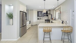 Uma cozinha moderna com uma ilha central, eletrodomésticos de aço inoxidável e dois banquetes de vime.