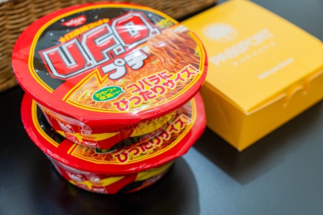 Uma pilha de alimentos embalados em vermelho e amarelo, com texto em japonês nos rótulos.