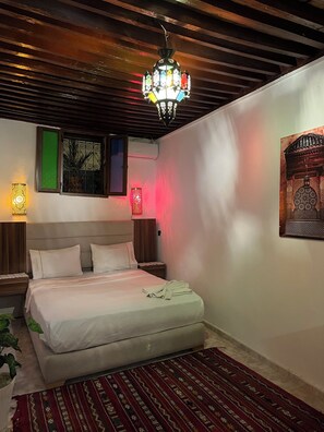 Quarto com cama, mesas de cabeceira, luminária pendente, ar-condicionado fixado na parede e tapete estampado.