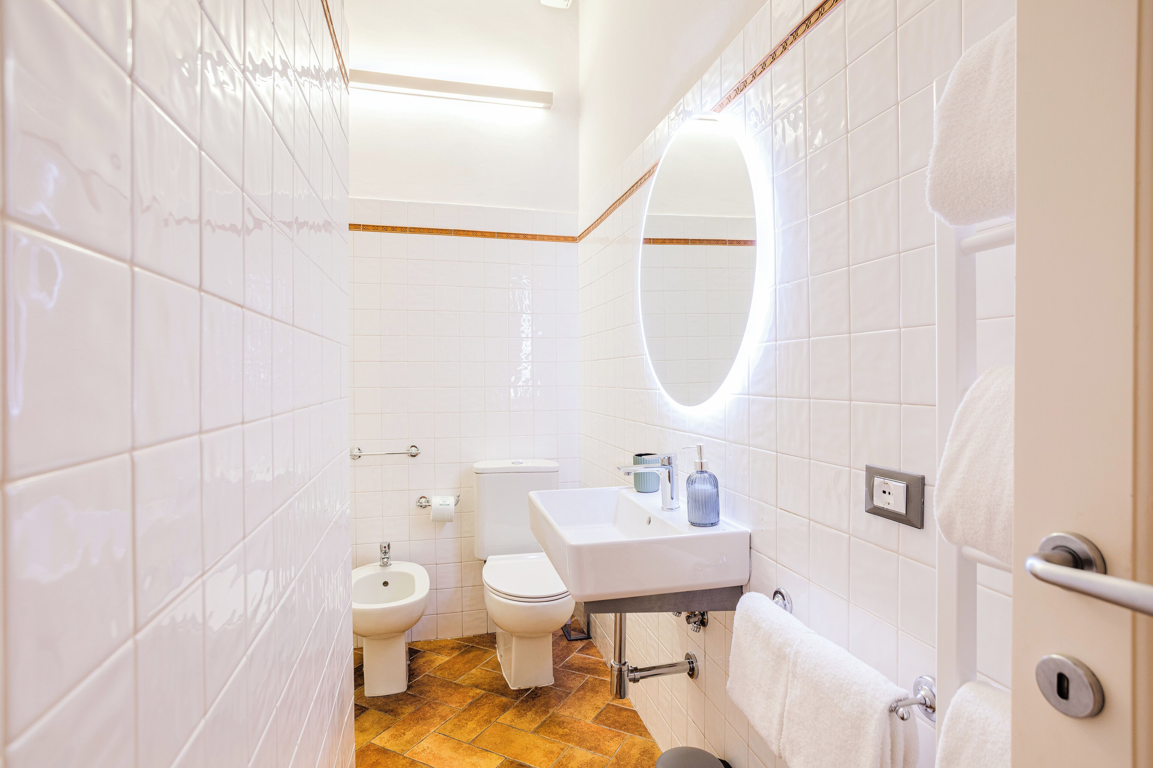 Casa de banho moderna com azulejos brancos, lavatório branco, espelho e sanita.