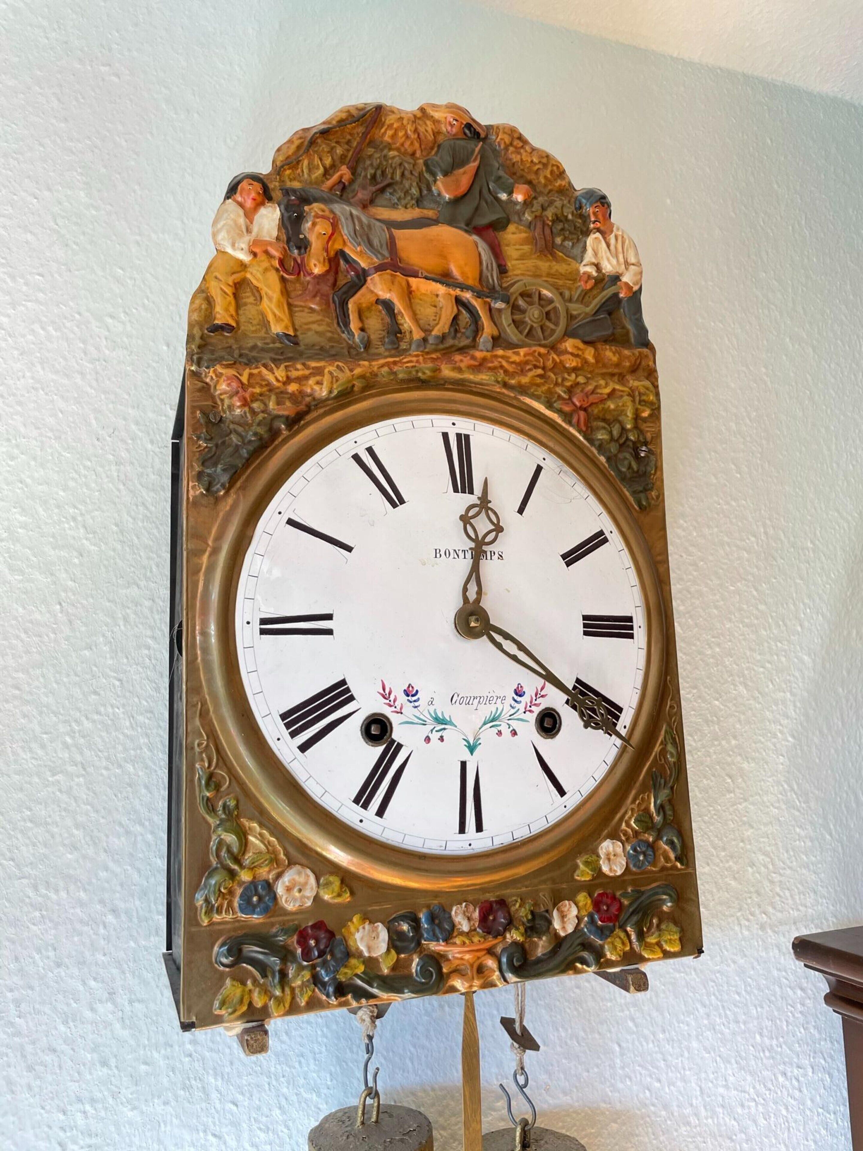 Um relógio fixado na parede, com moldura de madeira detalhada e detalhe decorativo superior.