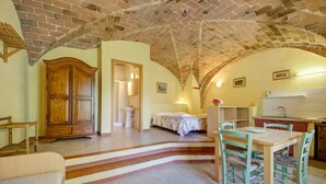 Um quarto espaçoso com teto de tijolos em arco, um armário de madeira, uma cama com colcha estampada, uma mesa de jantar com cadeiras e uma cozinha com pia e bancada.