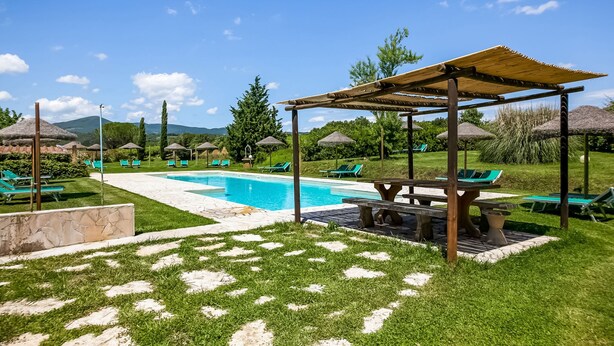 Área de piscina com espreguiçadeiras, pérgola e um caminho de pedra.