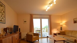 Uma sala de estar ampla com piso de madeira, um sofá, uma mesa de centro e uma televisão em um móvel de madeira.
