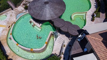Vista aérea de um resort com várias piscinas, uma grande estrutura tipo guarda-sol e uma área de estar coberta.