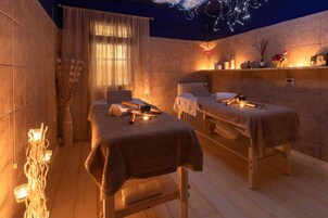 Um espaço de spa com duas macas de massagem, velas e objetos decorativos nas prateleiras.