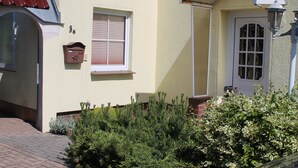 Uma casa com caixa de correio, janela com persianas, porta e um pequeno jardim.