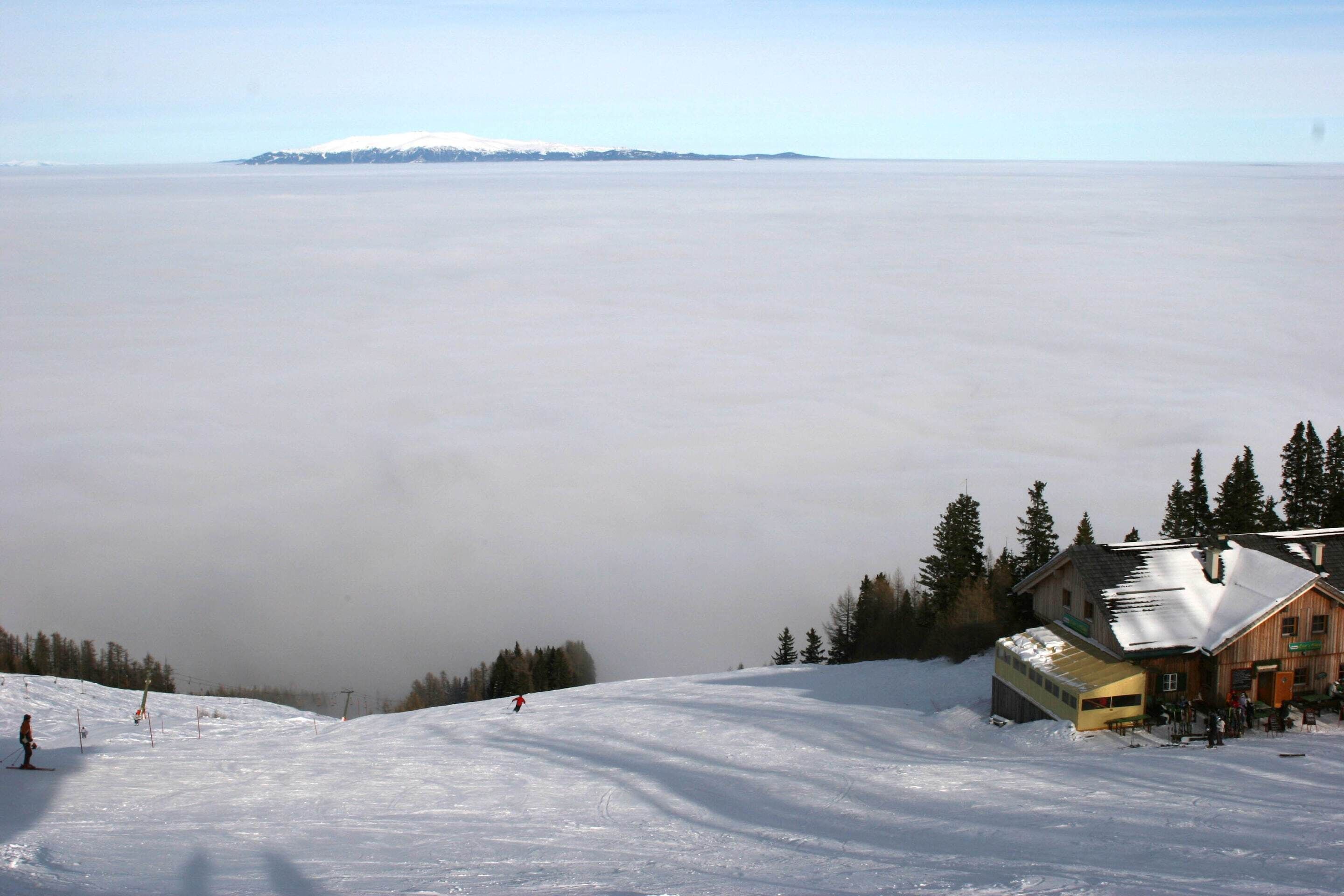 Montanha coberta de neve com uma cabana de madeira e vista clara do horizonte.