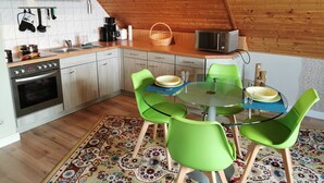 Uma cozinha com teto de madeira, fogão, micro-ondas e área de refeições com cadeiras verdes e mesa de vidro.