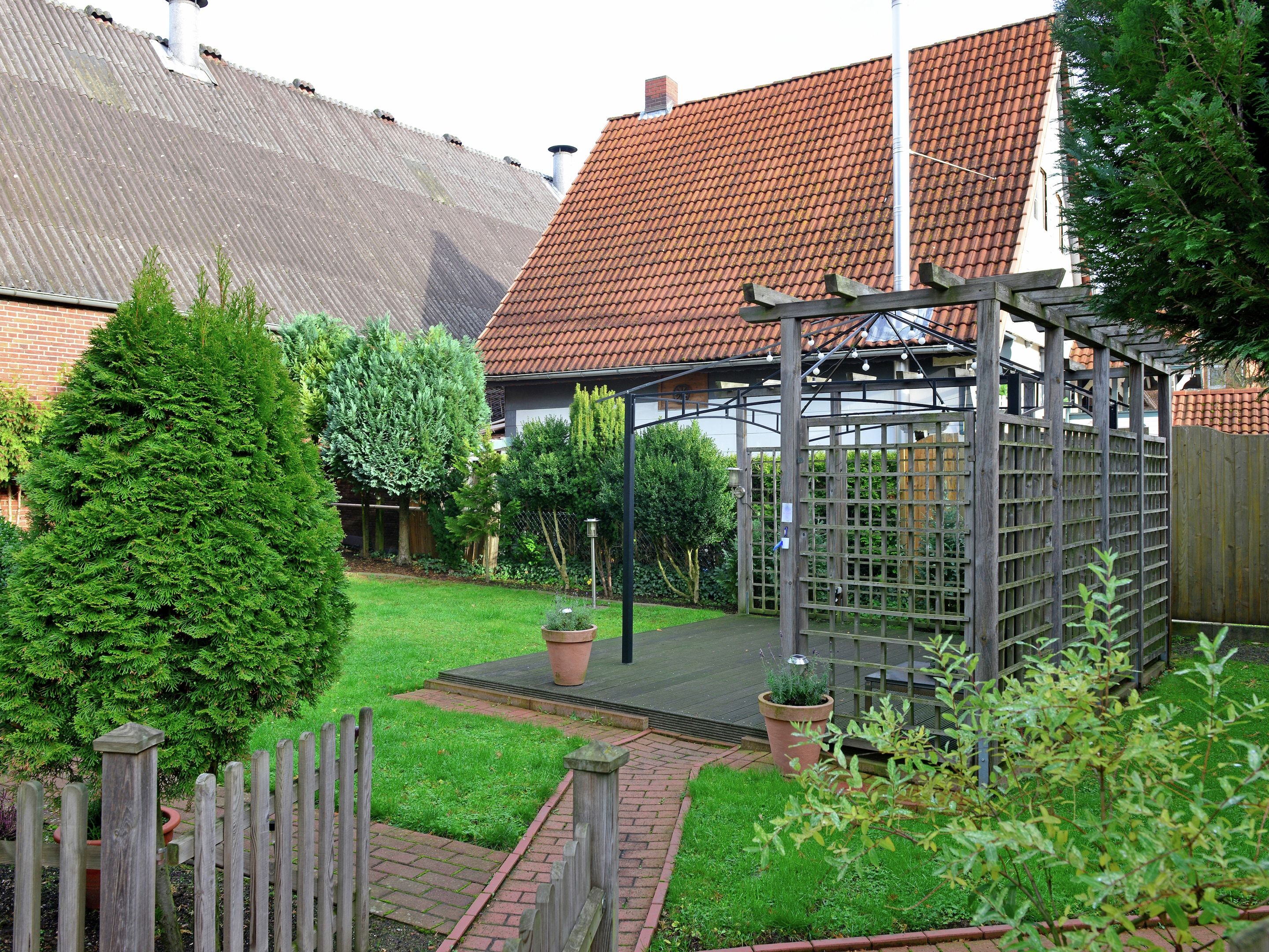 Um jardim com pérgola de madeira, caminho de tijolos e diversas plantas.