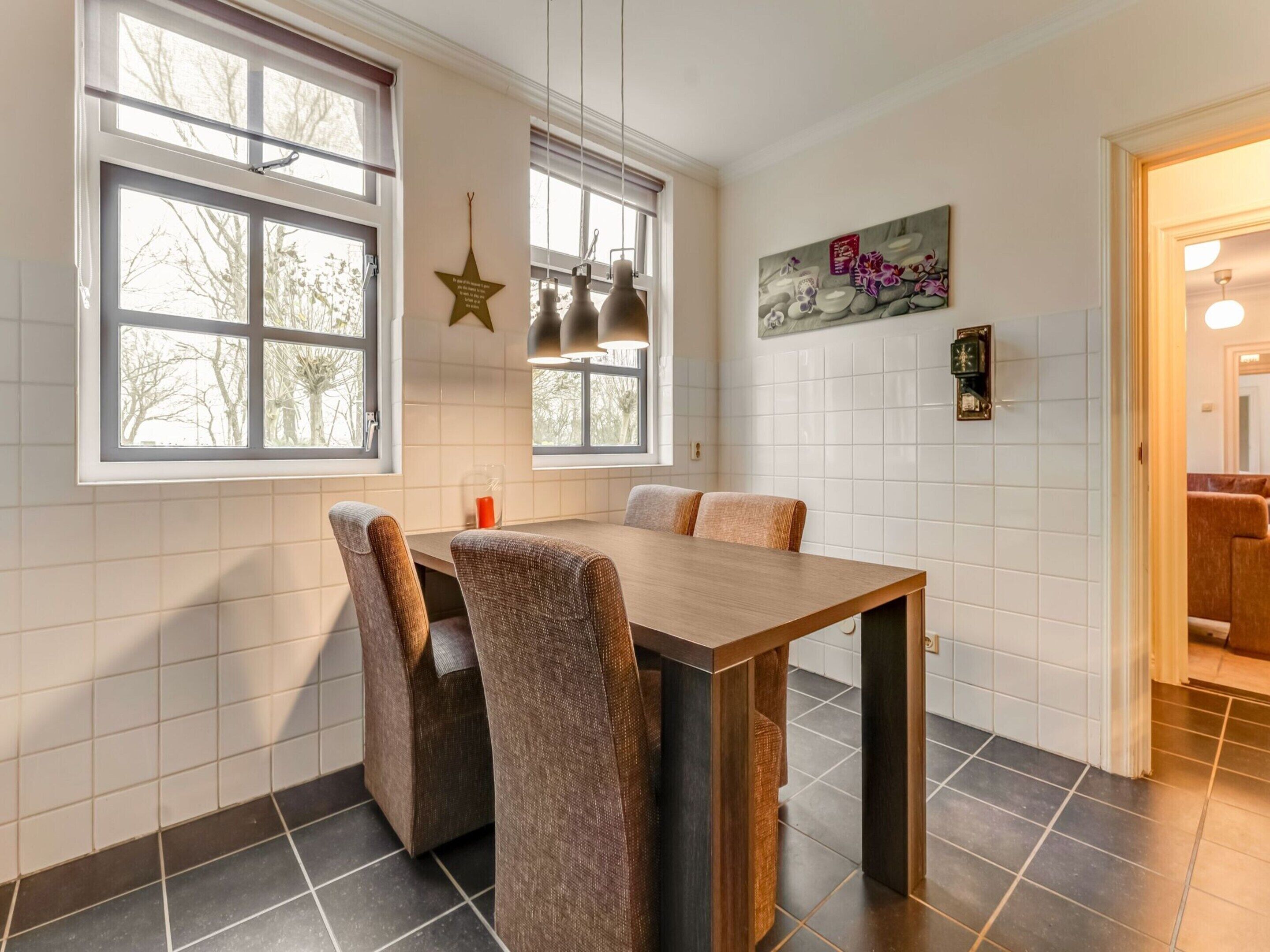 Uma cozinha moderna com uma mesa de jantar e cadeiras de madeira, janelas amplas e uma estrela decorativa na parede.