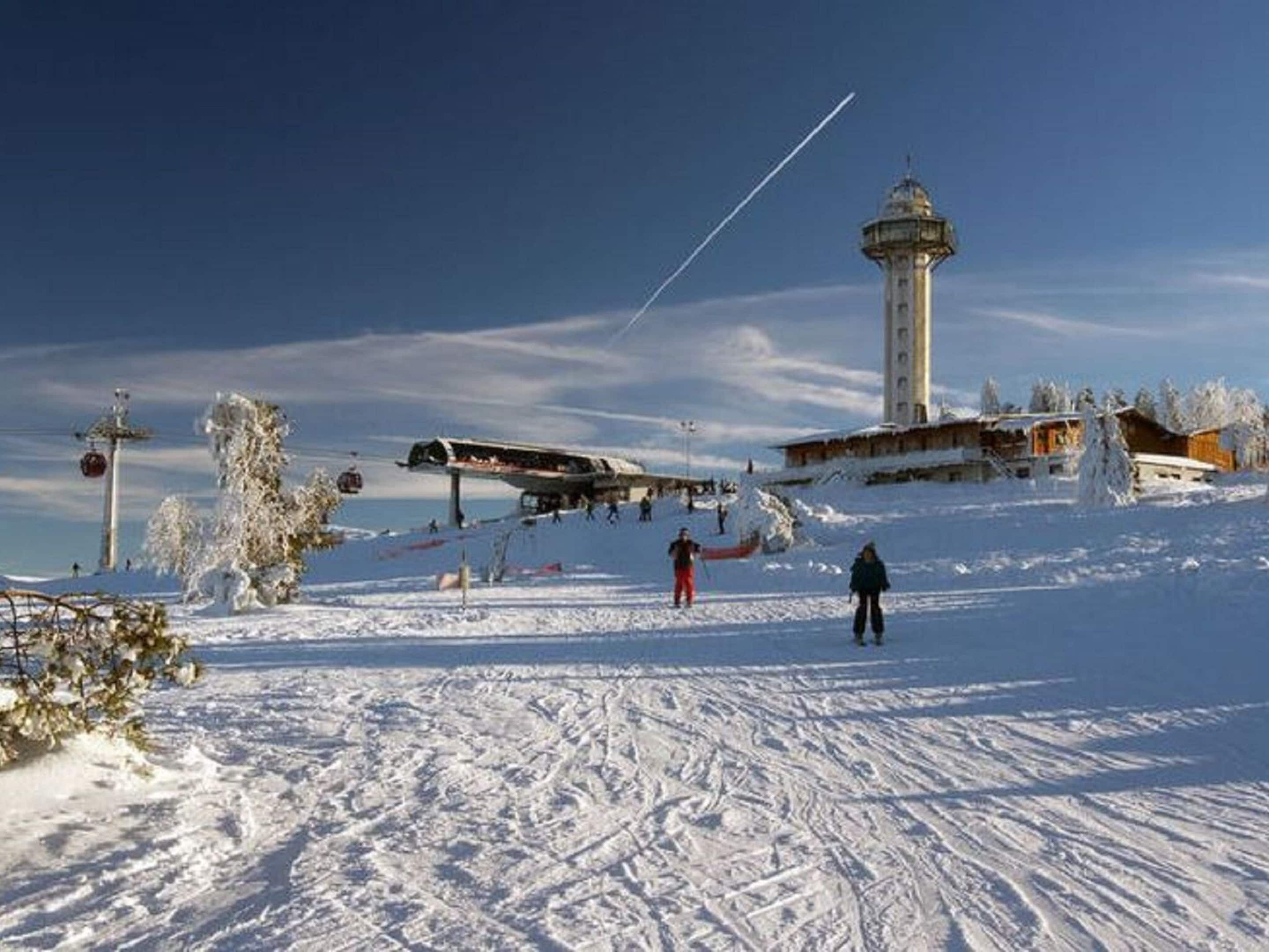 Pista de esqui coberta de neve com um teleférico, um farol e um edifício com telhado inclinado.