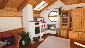 Interior acolhedor de uma cabana com vigas de madeira, lareira, sofá, área de jantar e um armário de madeira grande.