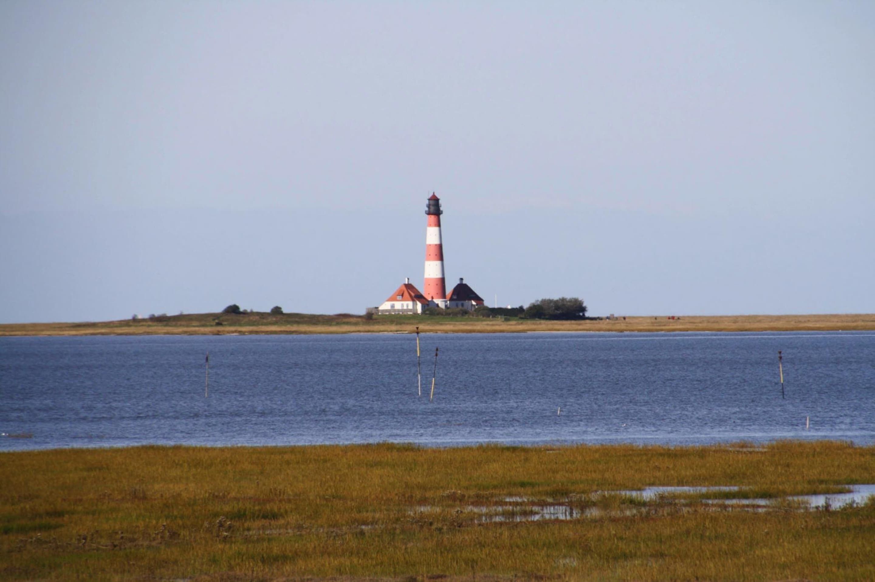 Um farol numa pequena ilha com vista clara para a água e terreno gramado ao redor.