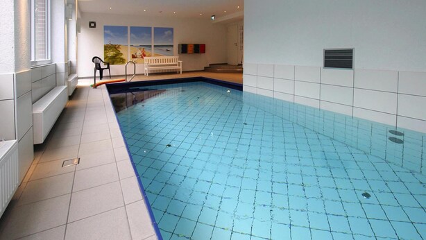 Piscina interna com paredes azulejadas e um banco perto da janela.