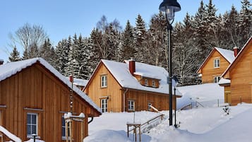Cabanas de madeira com telhados cobertos de neve e um poste de luz em uma paisagem nevada.