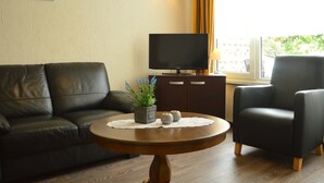 Sala de estar com sofá de couro, mesa de centro de madeira, televisão em um móvel de madeira e janela com cortinas.